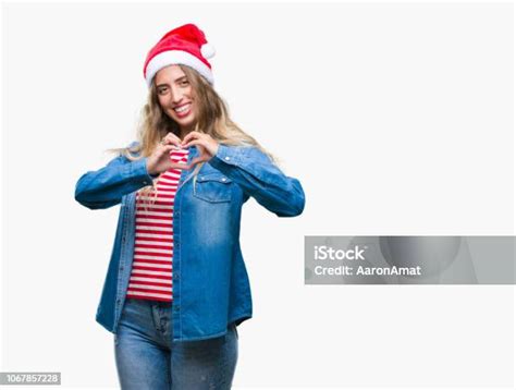 아름 다운 젊은 금발 여자 마음 기호와 손으로 모양을 보여주는 사랑에 웃 고 고립 된 배경 위에 크리스마스 모자를 쓰고 낭만적인