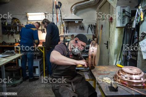 워크샵에서 황동 세부 사항을 확인 하는 보호 앞치마를 착용 하는 수동 노동자 다른 사람들이 배경에서 다른 작업을 수행 할 때 45 49세에 대한 스톡 사진 및 기타 이미지