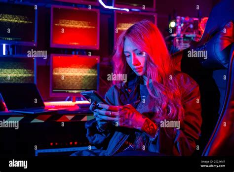 Asian Woman In Front Of A Computer Monitor Display Using Mobile Phone Neon Light Hacker Wear