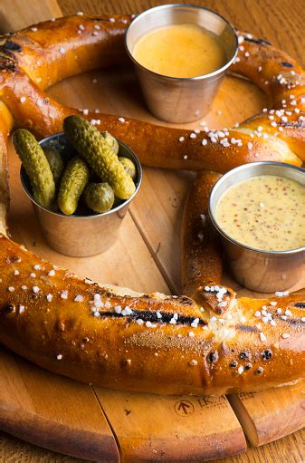 프레첼 나무 도마에 굵은 소금을 곁들인 갓 구운 부드러운 프레첼 통곡물 겨자 코니콘 피클 꿀 겨자와 함께 제공됩니다 근접 촬영 부드러움에 대한 스톡 사진 및 기타 이미지