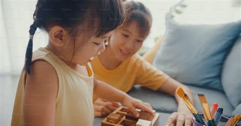 행복한 아시아 가족 엄마는 집 거실의 소파에서 휴식을 취하는 나무 상자로 소녀에게 보드 게임 취미를 가르칩니다 함께 시간 보내기 사회적 거리두기 코로나바이러스 격리