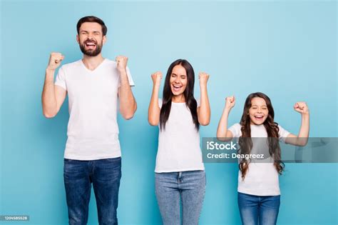 갈색 머리를 가진 기쁘게 엄마 아빠 소녀의 초상화 축하 승리 제기 주먹 비명 예 파란색 색상 배경 위에 고립 된 흰색 티셔츠 데님 청바지를 착용 T 셔츠에 대한 스톡 사진