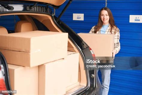 창고에 있는 차 트렁크 근처에 골판지 상자를 들고 있는 행복한 아가씨 25 29세에 대한 스톡 사진 및 기타 이미지 25 29세 30 34세 Brand Name