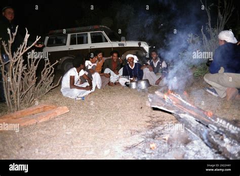 A Group Of Young Men Is Sitting And Chatting Around A Campfire In Front