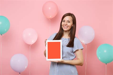 다채로운 공기 풍선 파스텔 핑크 배경에 빈 빈 화면 태블릿 Pc 컴퓨터를 들고 파란 드레스를 입고 웃는 매력적인 젊은 여자의 초상화 생일 휴가 파티 개념 14에 대한 스톡