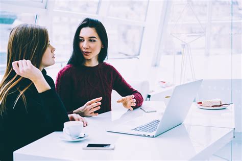 현대 장치와 커피 한 잔흰색 테이블에 앉아 비공식 회의에 친근한 대화 를하는 동안 서로 의사 소통 트렌디 한 의상을 입고 젊은 아름다운 힙스터 소녀 2명에 대한 스톡 사진