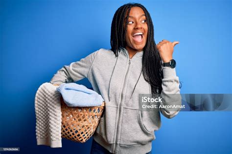 젊은 아프리카 계 미국인 소녀 하 고 국내 집안일 들고 빨래 고리 버들 바구니 가리키는 고 행복 한 얼굴 미소와 함께 측면에 엄지 손가락으로 표시 빨래에 대한 스톡 사진 및