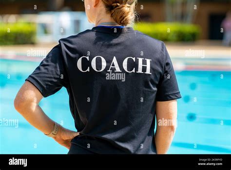 Back View Of Female Swimming Coach Wearing Coach Shirt Working At An Outdoor Swimming Pool