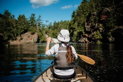 Woman Paddling A Canoe On A River Alongside A Pine Forest Stock Image