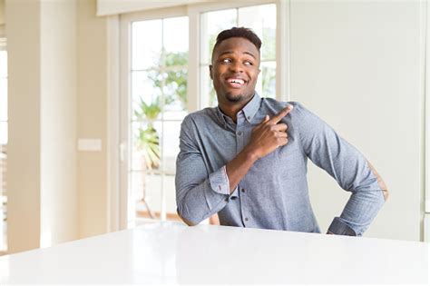 흰색 테이블에 잘생긴 아프리카계 미국인 남자 얼굴과 얼굴에 행복 하 고 자연 스러운 표정으로 측면에 손가락을 가리키는 미소와 쾌활 한 가리키기에 대한 스톡 사진 및 기타