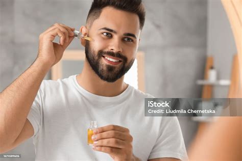 잘 생긴 남자가 실내 거울 근처에서 얼굴에 화장품 세럼을 바르고 있습니다 20 24세에 대한 스톡 사진 및 기타 이미지 20 24세 건강한 생활방식 깨끗한 Istock