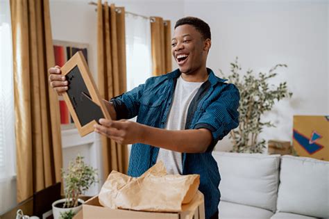 한 남자가 새 아파트로 이사한 후 거실에서 청소하고 골판지 상자를 풀고 소년은 어린 시절부터 프레임에 있는 사진을 발견하고 충격을 받고 기쁨으로 시계를 보냅니다 가구에 대한