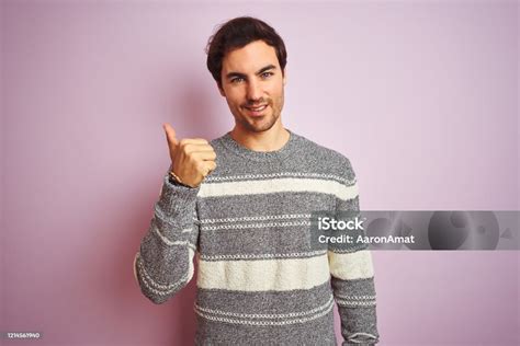 젊은 잘 생긴 남자 캐주얼 줄무늬 스웨터를 입고 고립 된 분홍색 배경 위에 서 행복 한 엄지 손가락 을 하 고 손으로 제스처