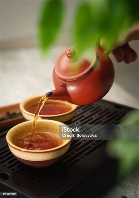 여성의 손이 이싱 점토 찻주전자에서 도자기 찻잔에 차를 붓고 고요한 차 의식을 만듭니다 부드러운 조명 나무 찻잔 및 녹지는 차분한 마음 챙김 Chenese 의식 분위기를