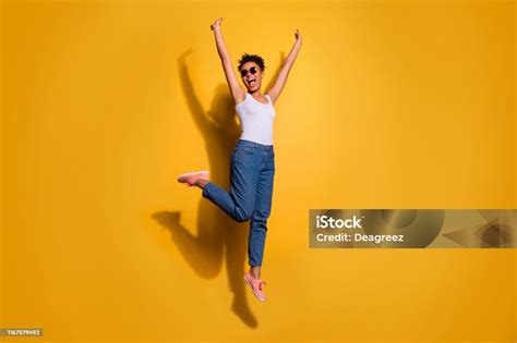 전체 길이 바디 크기 사진 아름다운 그녀 그녀의 어두운 피부 흥분 여자 점프 높은 소리 예 승리 챔피언 착용 캐주얼 청바지 데님 바지 바지 탱크 탑 고립 밝은 노란색 배경