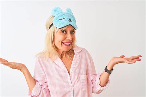 파란 수면 마스크와 잠옷을 입은 중년 여성은 고립 된 흰색 배경에 팔과 손을 들고 혼란스러운 표정을 짓고 있습니다 의심 개념 감정에 대한 스톡 사진 및 기타 이미지 Istock