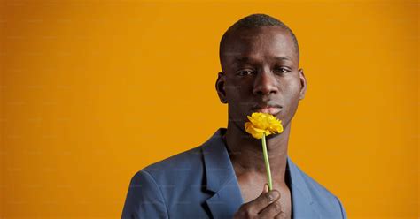 양복을 입은 아프리카 잘생긴 남자가 노란색 배경에 고립된 꽃을 들고 카메라에 포즈를 취하는 초상화 사진 Unsplash의 양복 이미지