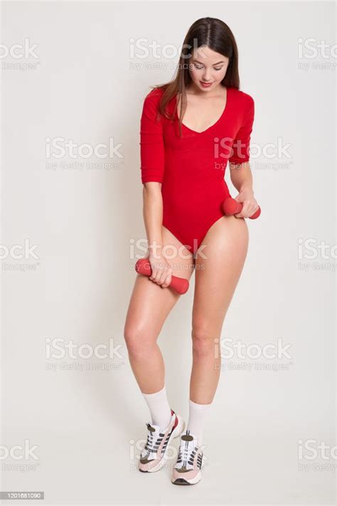 빨간 스포츠 콤비 드레스 흰색 양말과 운동화를 입고 아령을 들고 아래를 내려다 보며 스튜디오에서 흰색 배경 위에 고립 된 귀여운