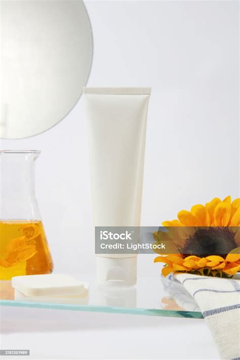 유리 카운터에는 라벨이 없는 흰색 튜브와 여전히 빈 공간 노란색 액체와 꽃잎이 들어 있는 삼각 튜브 해바라기와 목욕 수건이 들어 있었습니다 디자인을 위한 빈 공간 전면 모습