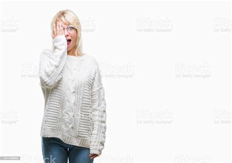 젊은 아름 다운 금발 여자 얼굴과 놀라운 감정에 확신 미소와 함께 손으로 한쪽 눈을 덮고 격리 된 배경 위에 겨울 스웨터와 안경 착용 가리기에 대한 스톡 사진 및 기타