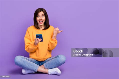 젊은 여성 블로거 인플 루 언서의 전신 크기 사진 보류 스마트 폰 앉아있는 손가락 포인트 빈 공간 전자 쇼핑 프로모션 보라색 배경에 고립 20 24세에 대한 스톡 사진 및