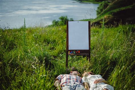 깨끗한 흰색 캔버스가 있는 나무 이젤은 강과 하늘을 배경으로 녹색 잔디밭에 서 있습니다 텍스트 와 디자인을 위한 장소 러브 스토리 2명에 대한 스톡 사진 및 기타 이미지