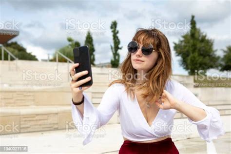 여름에 밖에서 셀카를 찍기 위해 휴대 전화를 사용하여 돌 계단에 앉아있는 젊은 여성 20 24세에 대한 스톡 사진 및 기타