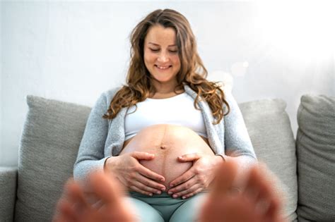 소파에 앉아 행복한 미소를 짓는 여자가 임신 마지막 단계에서 아기를 낳을 것을 기대하며 부드럽게 배를 잡고 있는 모습 임신 3 분기 34 주 정면도 흰색 배경입니다 임신에