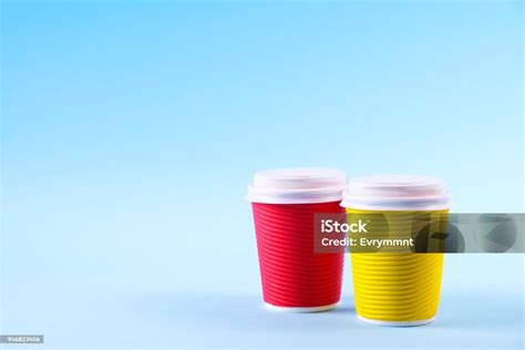 밝은 빨간색 및 노란색 이중의 쌍 벽으로 종이 컵 테이크아웃 커피가 게 모자 파란 배경에 승 뜨거운 음료에 대 한 두 개의 다채로운 환경 친화적인 열 증거 판지 머그잔을