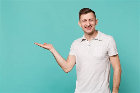서 있는 캐주얼 복장에서 쾌활 한 젊은 남자의 초상화 스튜디오에서 파란색 청록색 벽 배경에 고립 된 손을 옆으로 가리키는 사람들은 진심으로 감정 라이프 스타일 개념입니다