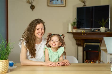 행복한 미소 가족의 초상화 테이블에 엄마와 딸이 카메라를 본다 두 자매는 웃는다 집에서 방에 앉아서 웃음 텍스트에 대 한 배치 행복한 어린 시절 여자와 소녀 에 이 프레임