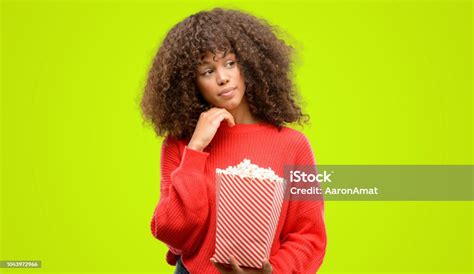 아프리카계 미국인 여자 먹는 팝콘 심각한 얼굴 생각 질문 매우 혼란 스 러 워 아이디어에 대 한 팝콘에 대한 스톡 사진 및 기타 이미지 Istock