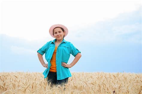 잘 익은 밀이 있는 밭에는 햇볕이 잘 드는 모자를 쓰고 허리에 손을 얹은 예쁜 소녀가 서서 미소를 짓고 있습니다 25 29세에 대한 스톡 사진 및 기타 이미지 Istock