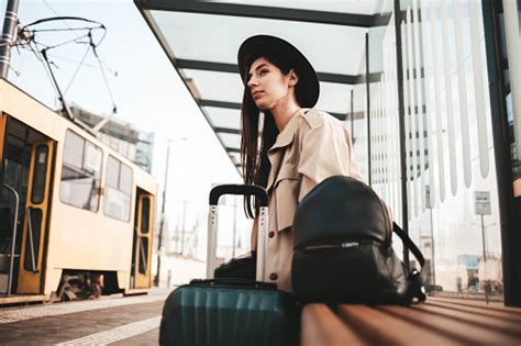 슬픈 얼굴을 가진 코트와 모자를 쓴 젊은 여행자 여성이 혼자 버스 시티 정류장에 앉아있습니다 가방에 대한 스톡 사진 및 기타 이미지 Istock