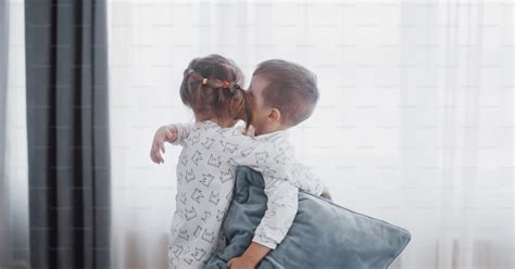 하얀 침실에서 노는 행복한 아이들 어린 소년과 소녀 형제와 자매는 잠옷을 입고 침대에서 놀고 있습니다 어린이를위한 보육원 인테리어 아기와 유아를 위한 잠옷과 침구