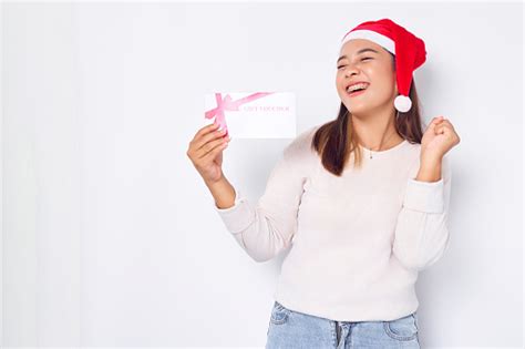 산타클로스 모자를 쓴 즐거운 젊은 아시아 여성 20대가 상점에 대한 상품권 쿠폰 카드를 들고 흰색 스튜디오 배경에 고립된 승자 제스처를 하고 있다 25 29세에 대한 스톡
