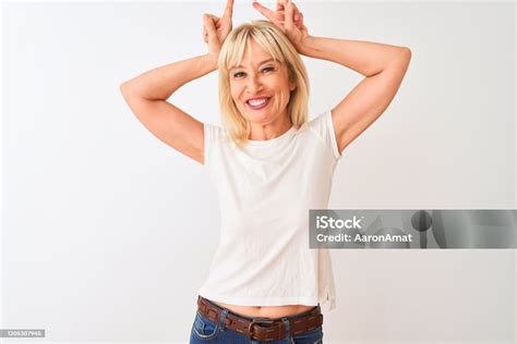 황소 뿔로 머리 위에 손가락으로 재미있는 제스처를하고 고립 된 흰색 배경 위에 서 캐주얼 티셔츠를 입고 중년 여성 T 셔츠에