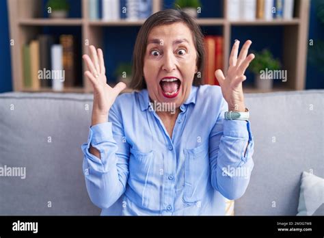 Middle Age Hispanic Woman Sitting On The Sofa At Home Celebrating Crazy