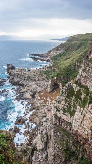 흐린 하늘 아래 무성한 녹지와 부서지는 파도가있는 해안 절벽의 경치 좋은 전망 0명에 대한 스톡 사진 및 기타 이미지 0명