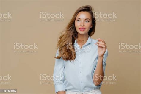 긴 머리를 가진 사랑스러운 여자를 기쁘게 손을 들고 세련된 셔츠를 입고 조개 얼굴 표정을 가지고 기분 좋게 미소 갈색 배경에 대한 스튜디오에 서있다 사람과 패션 컨셉 갈색에
