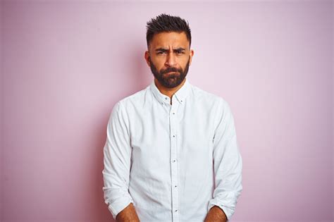 고립 된 분홍색 배경 회의론자 및 긴장 문제로 인해 눈살을 찌푸리는 화가 위에 서있는 우아한 셔츠를 입은 젊은 인도 사업가 부정적인 사람 감정에 대한 스톡 사진 및 기타