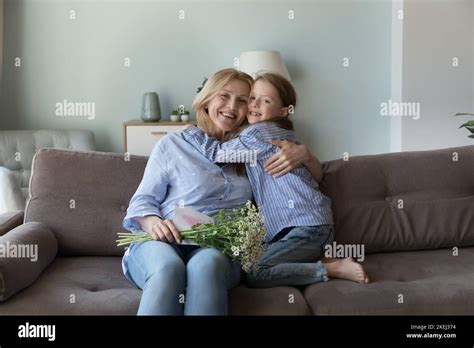 Happy Grandma Holds Flowers Hugs Granddaughter Smile Look At Camera
