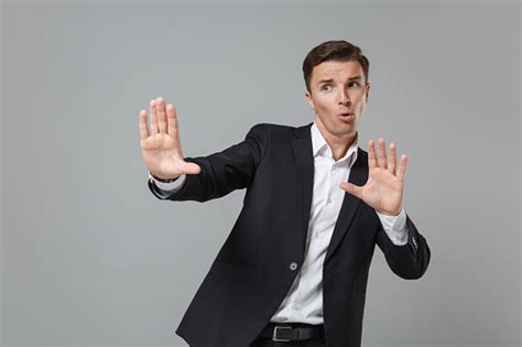 스튜디오에서 회색 배경에 고립 포즈 고전적인 검은 정장 셔츠에 젊은 사업가 를 충격 성취 경력 재산 사업 개념 복사 공간을 모의합니다 손바닥을 보여주는 손을 위로 올려