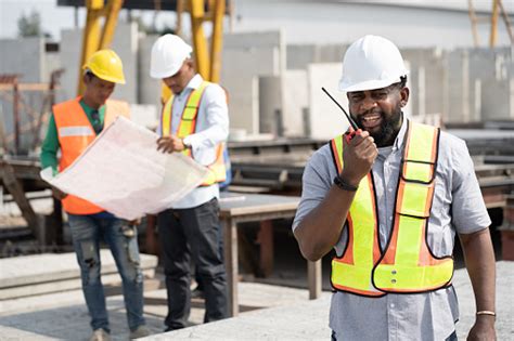 초상화 아프리카계 미국인 엔지니어 남자는 서류 작업과 프리캐스트 시멘트 공장 배경으로 작업하는 팀과 함께 워키토키를 사용합니다