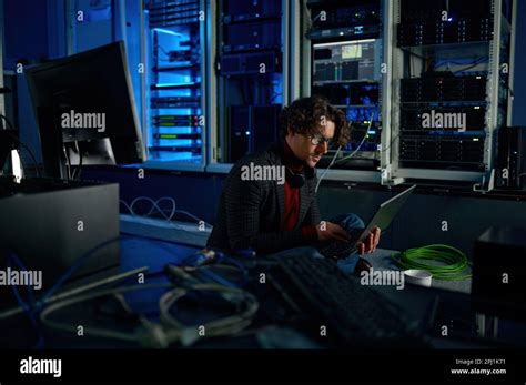 Male System Administrator Working In Server Room Using Laptop Stock