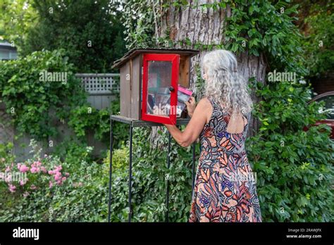 A Woman Checks Out Free Books At A Front Yard Little Library Which
