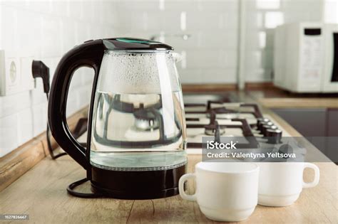 주방의 나무 테이블에 있는 현대적인 전기 투명 주전자 물을 끓이고 차를 만들기위한 주전자 뜨거운 음료를 만들기위한 가전 제품 복사 공간 텍스트를 위한 장소입니다 가정 생활에