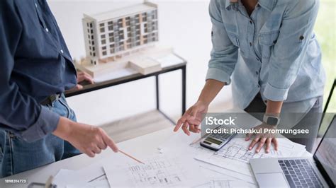 두 명의 엔지니어 건축가가 작업장 현장에서 함께 작업하면서 건축 계획과 건축 모형에 대한 기술에 대해 논의하기 위해 내부 건축 건물을 스케치하는 청사진을 가리키고 있습니다