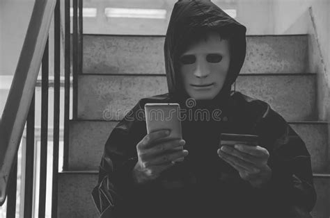 Anonymous Computer Hacker In White Mask And Hoodie Hacker Holding Credit Card And Using