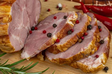 나무 도마에 육즙이 많은 돼지 고기 햄을 얇게 썬 조각 그 옆에는 조각 칼 멀티 컬러 피망 완두콩 붉은 고추 및 바질이 있습니다